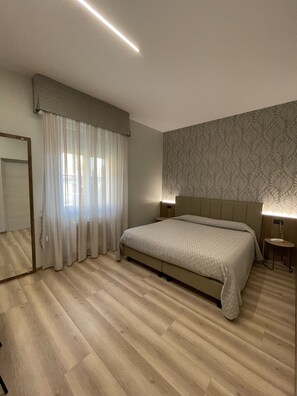Quarto com cama, mesa de cabeceira, espelho e papel de parede estampado.