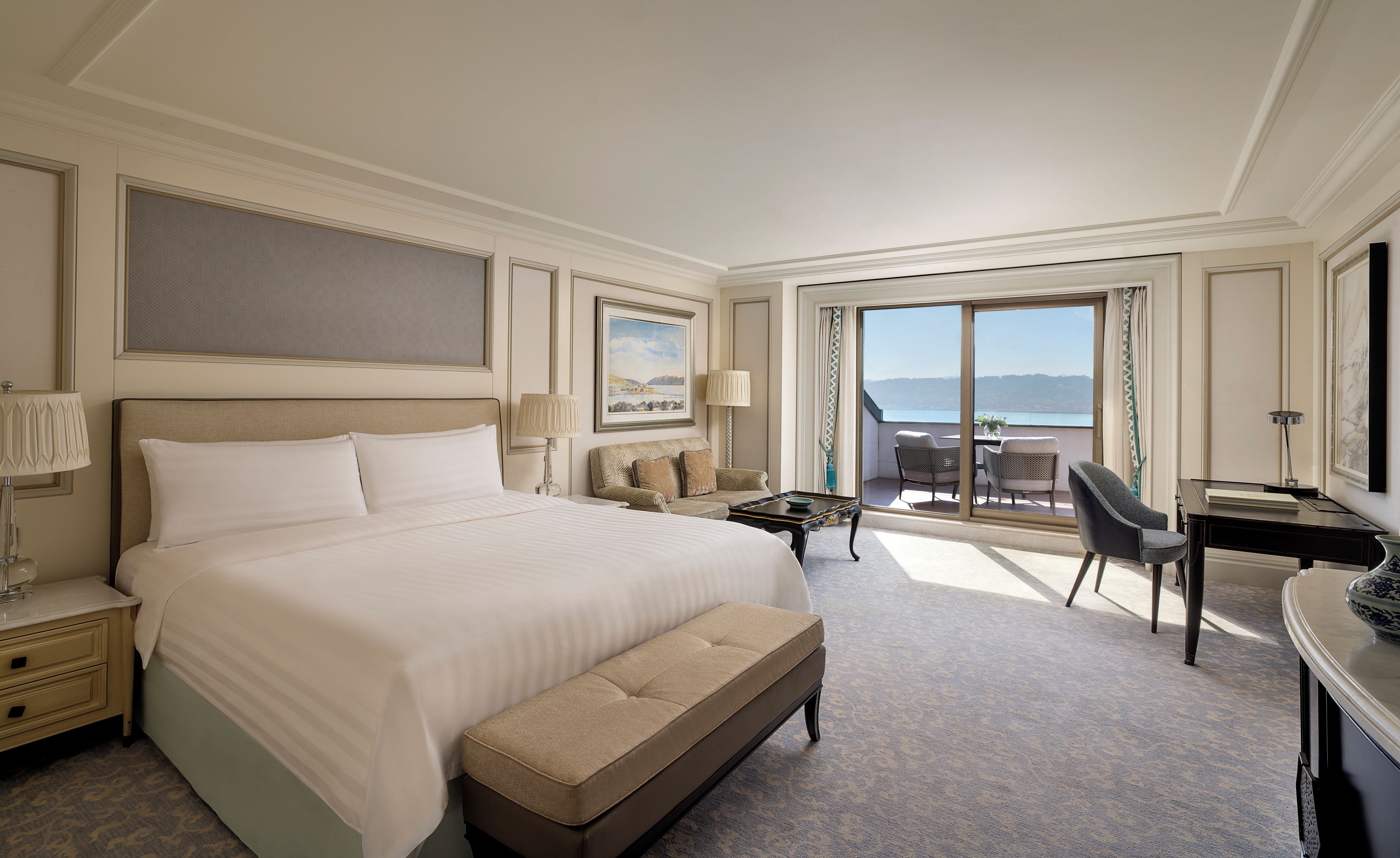Quarto de hotel com cama grande, escrivaninha, cadeira, banco e varanda com vista.