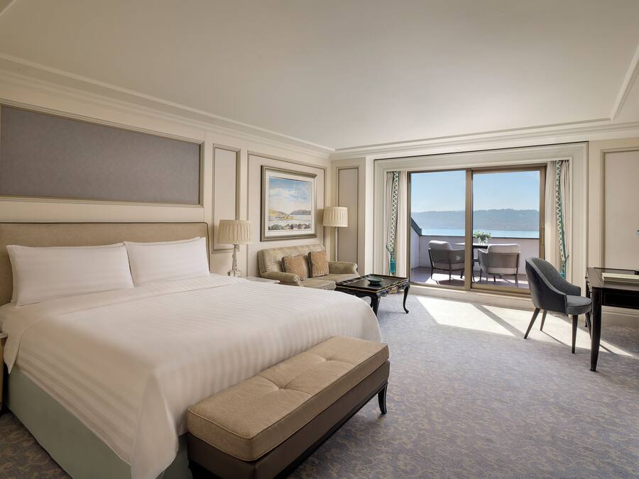 Quarto de hotel com cama grande, escrivaninha, cadeira, banco e varanda com vista.
