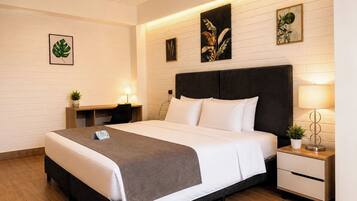 Quarto de hotel moderno com cama grande, mesas de cabeceira, escrivaninha e uma cadeira.
