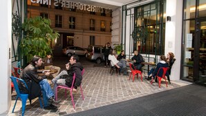 Um grupo de pessoas sentadas em mesas do lado de fora de um edifício, com uma placa que diz 'INTERIORS'.