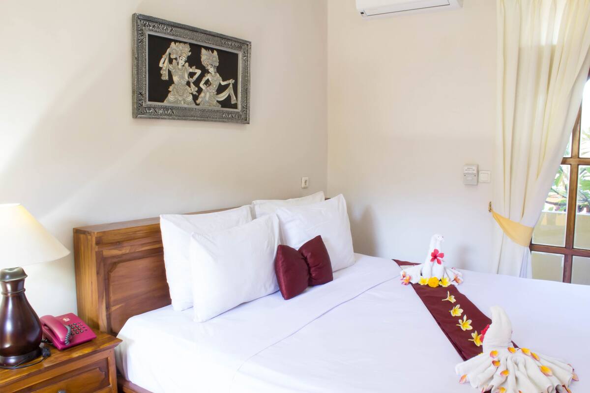Quarto de hotel com uma cama bem arrumada, um quadro na parede, um abajur e um telefone na mesa de cabeceira.