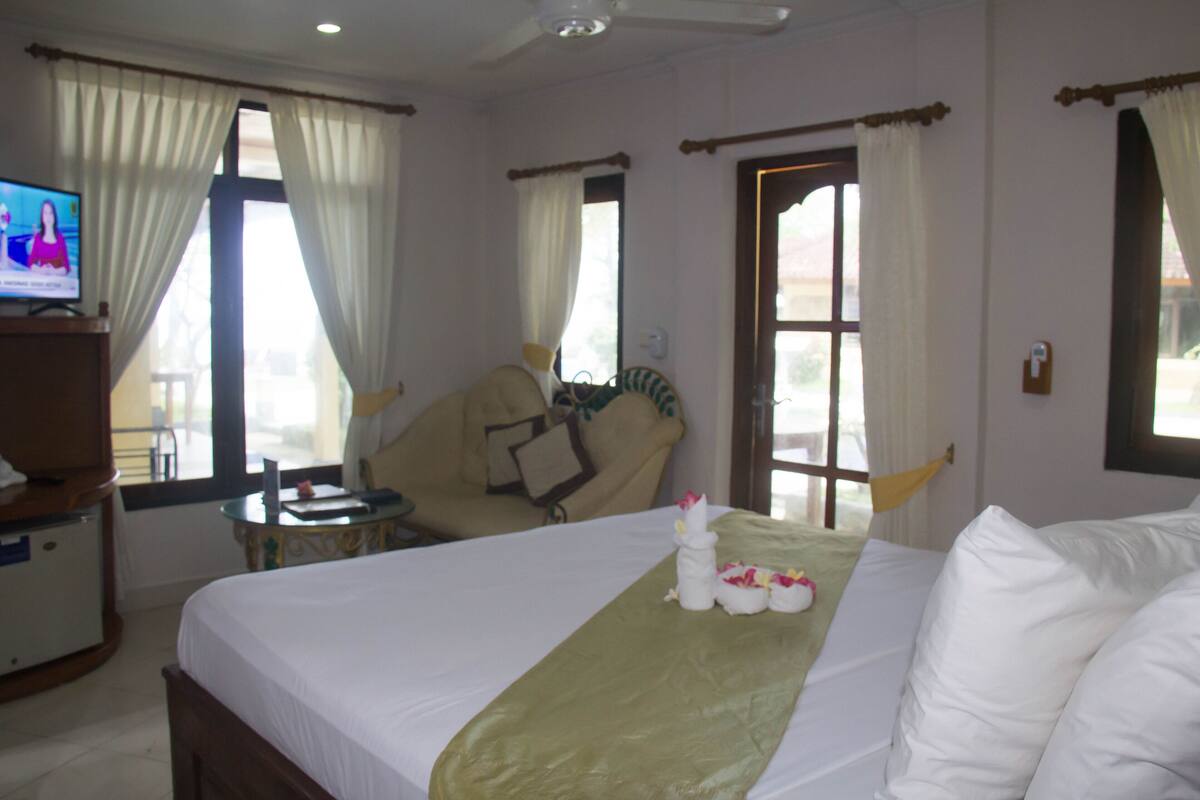 Quarto de hotel com cama, televisão, sofá e janela com cortinas.