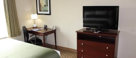Quarto de hotel com cama, escrivaninha com abajur, televisão e cómoda.
