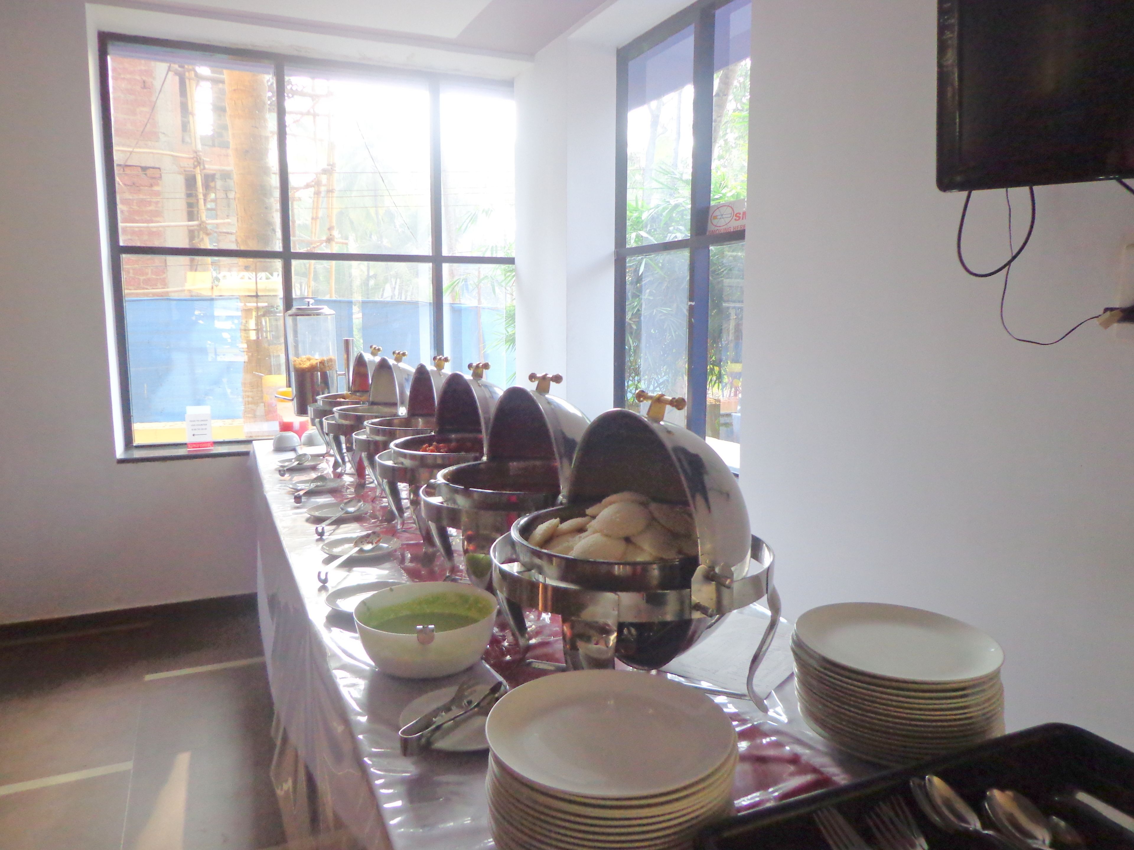 Disposição de buffet com vários recipientes de comida e uma grande janela com vista para edifícios e árvores.