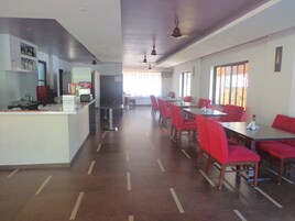 Um restaurante com um balcão comprido, cadeiras vermelhas e uma área de refeições com mesas.