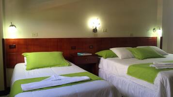 Duas camas de solteiro com roupa de cama verde e branca, cabeceira de madeira, mesas de cabeceira com luminárias e um aparelho de ar condicionado acima.