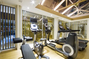 Academia com diversos equipamentos de exercício, amplas janelas e um design de teto moderno.