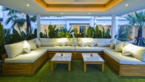 Uma área de estar moderna ao ar livre com sofá modular, duas mesinhas de centro e plantas tropicais exuberantes.