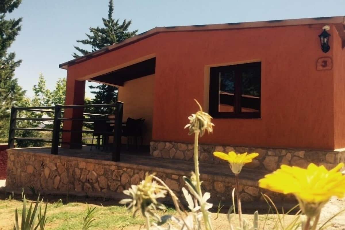 Um pequeno edifício térreo com alicerce de pedra e exterior vermelho. Há uma janela no lado direito e uma porta no lado esquerdo.
