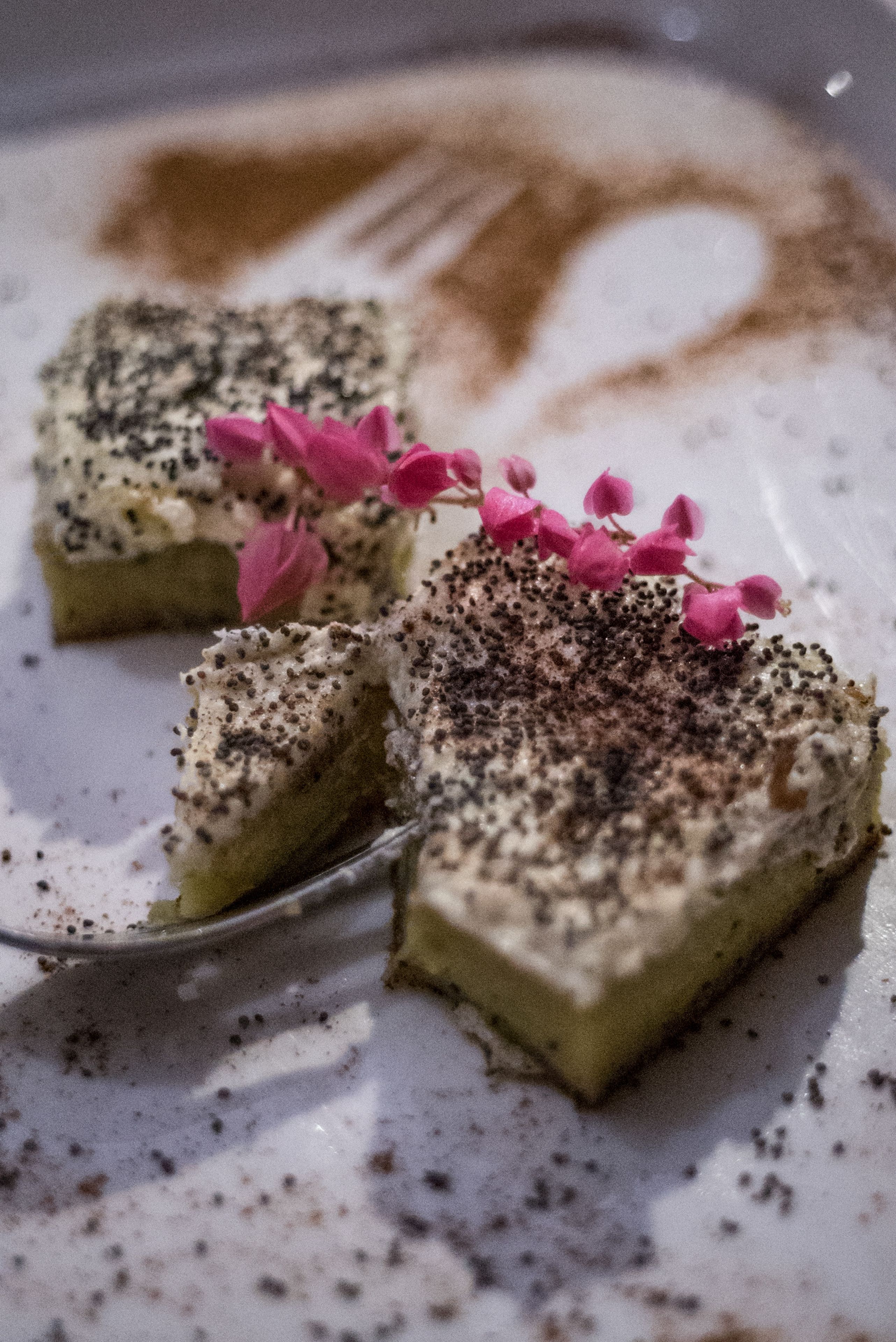Uma sobremesa com design em formato de coração, decorada com flores cor-de-rosa e salpicada com sementes pretas.