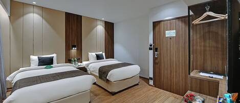 Quarto de hotel com duas camas, piso de madeira, escrivaninha com cafeteira e guarda-roupa.