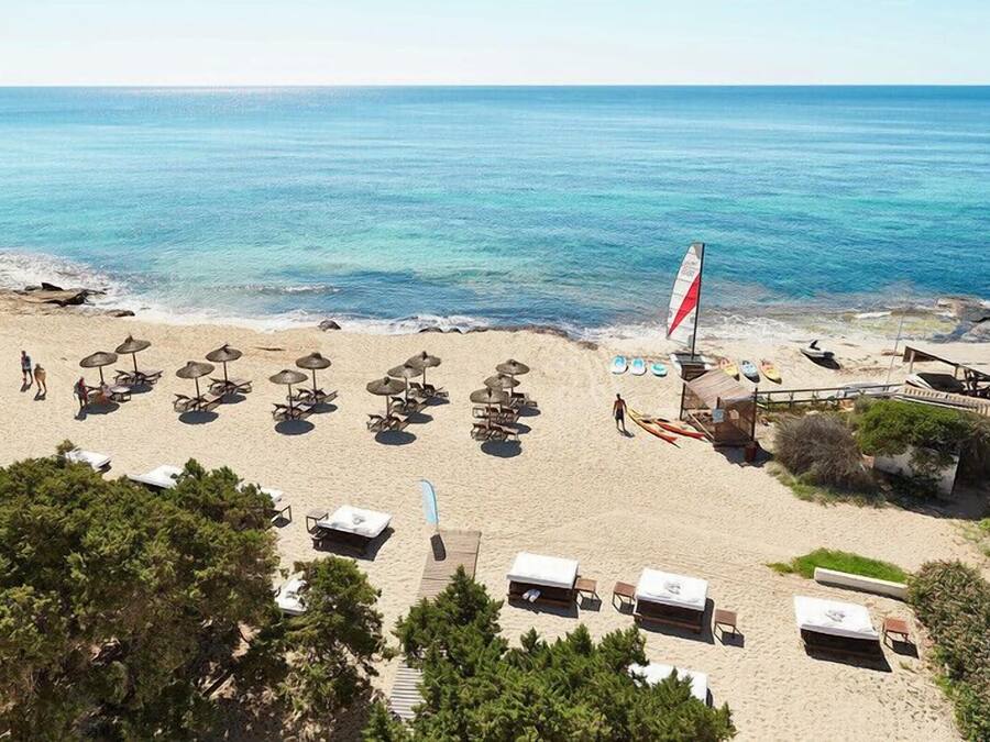 Uma praia com espreguiçadeiras, guarda-sóis e um veleiro.