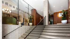 Um hall de hotel moderno com uma escadaria de mármore, painéis de madeira e plantas em vasos.