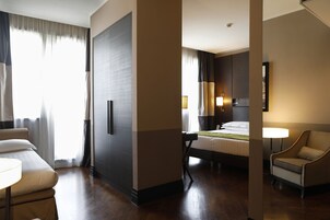 Quarto de hotel com uma cama, uma escrivaninha, uma cadeira e um espelho grande.