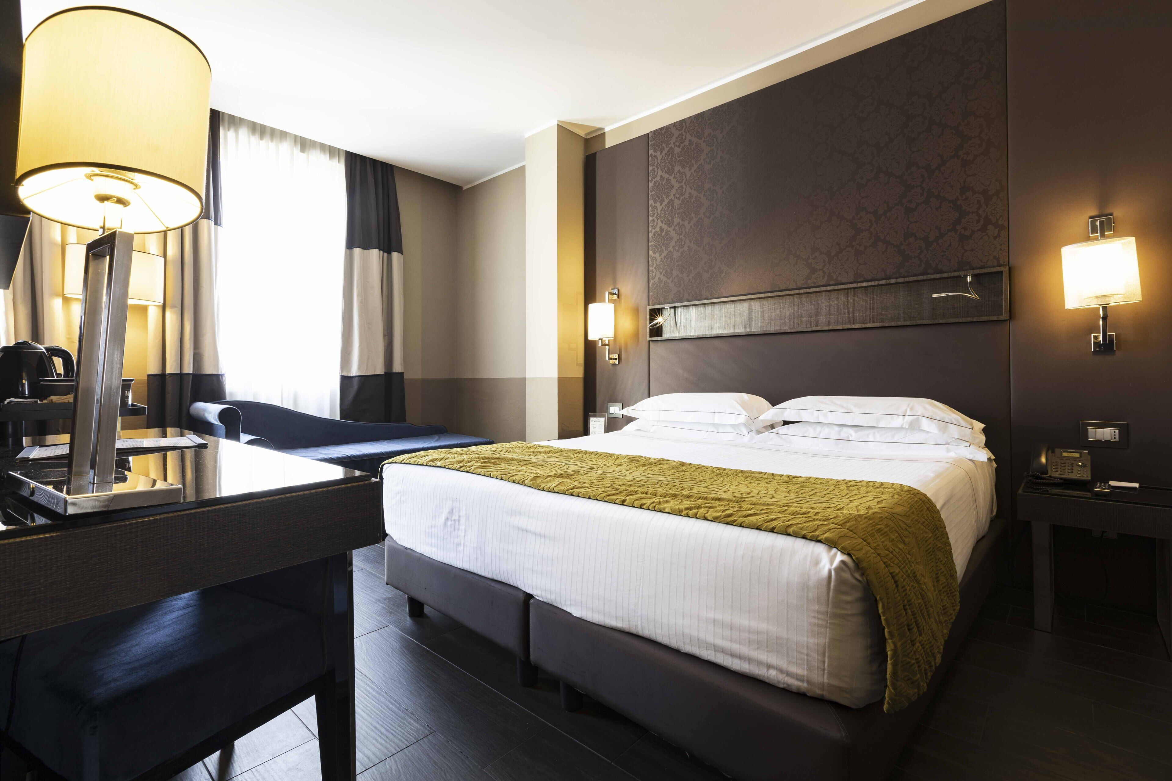 Quarto de hotel com cama, mesas de cabeceira, escrivaninha e abajur.