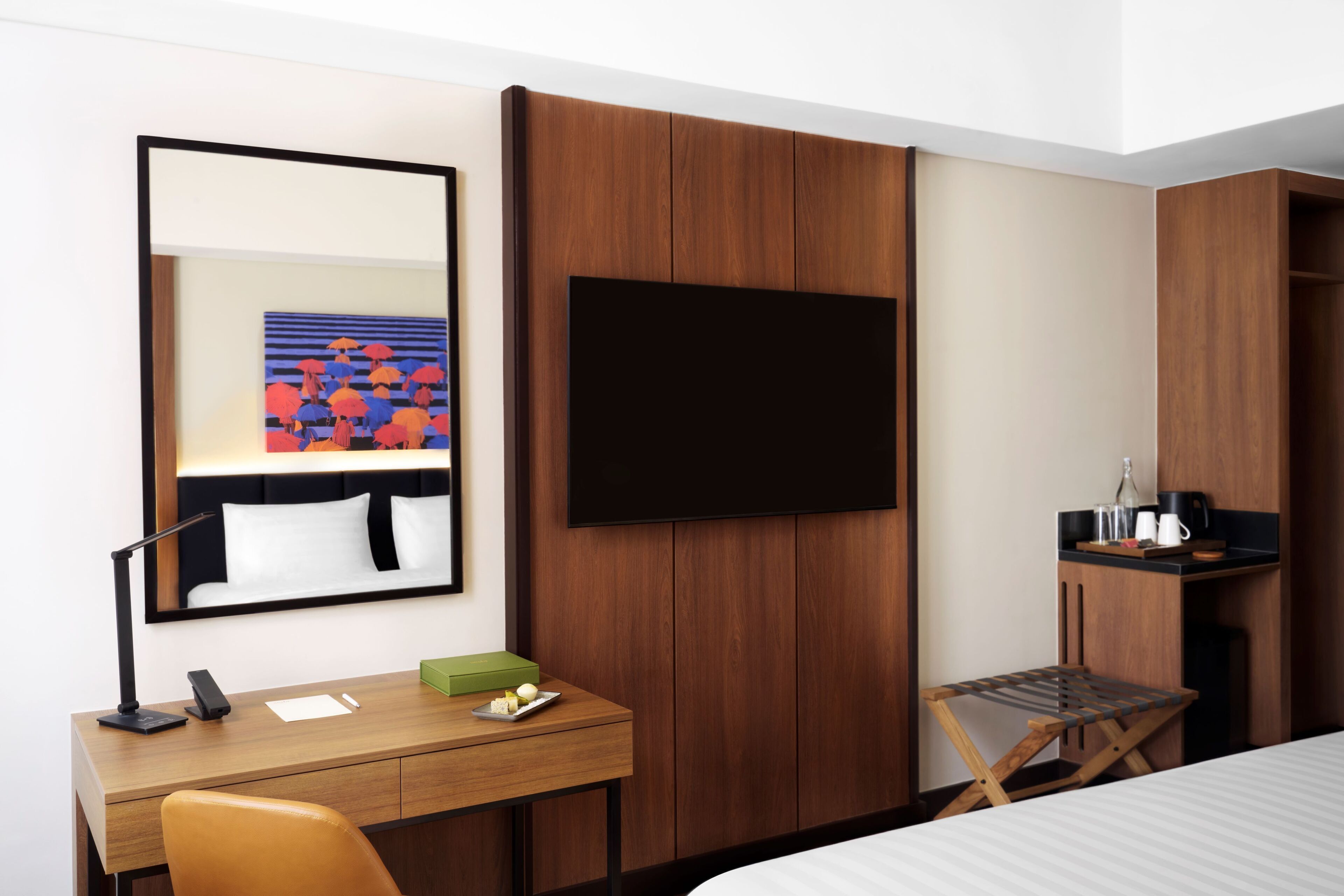 Quarto de hotel com escrivaninha de madeira, televisão de tela plana, cama e um pequeno espaço de estar.