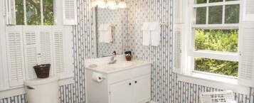 Casa de banho com toucador branco, janela e papel de parede estampado.