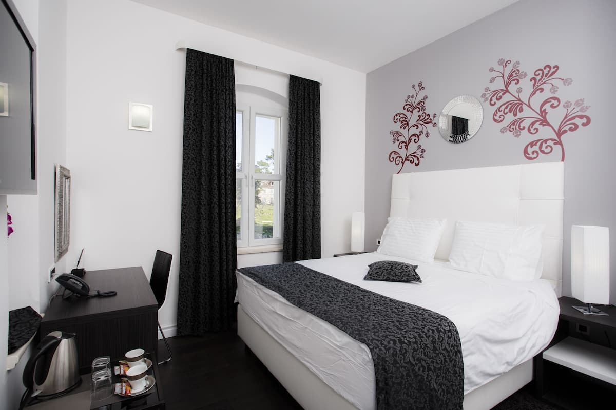 Quarto de hotel moderno com uma cama grande, uma mesa com telefone, uma cadeira e uma pequena mesa com chaleira e xícaras.