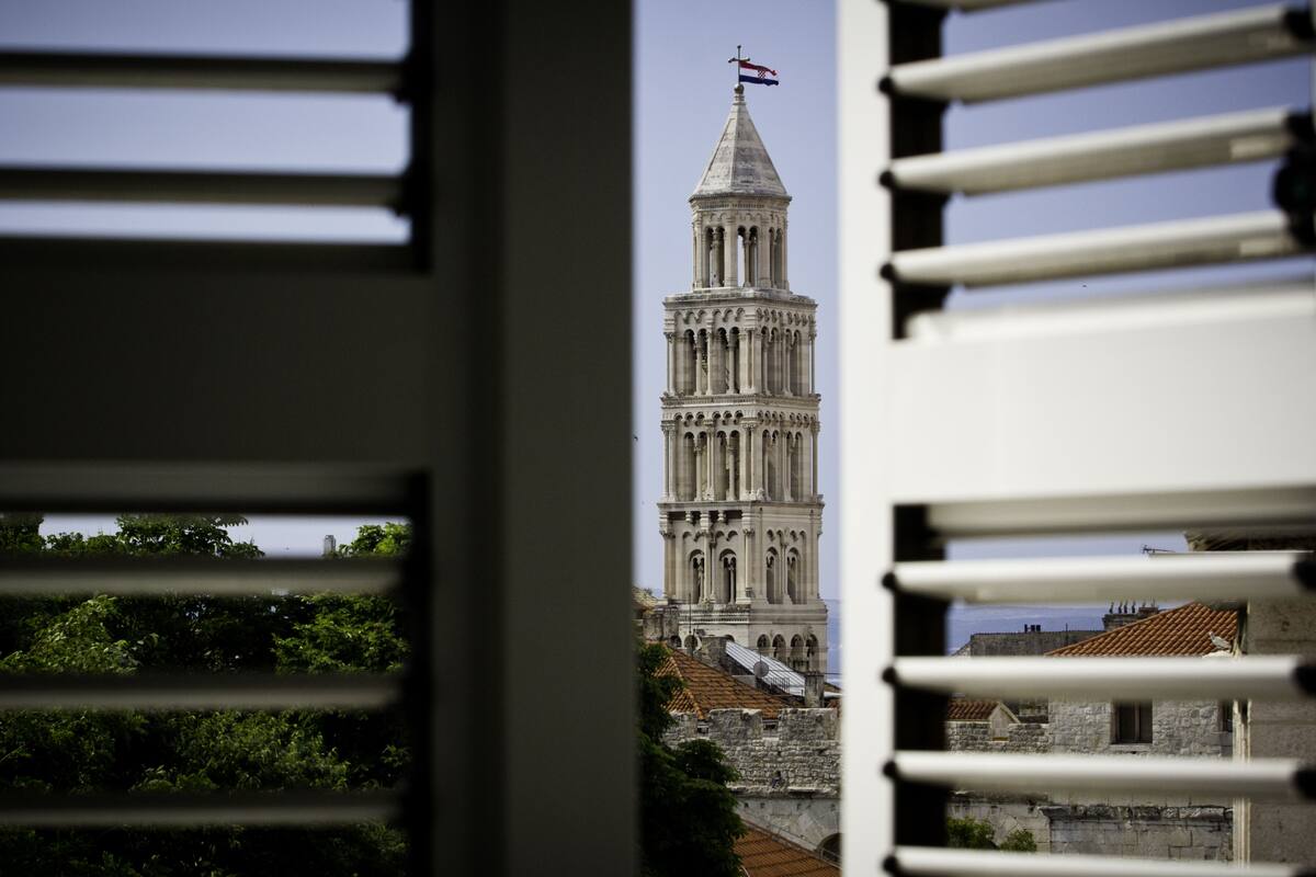 Vista de uma torre histórica com uma bandeira, vista através de venezianas.