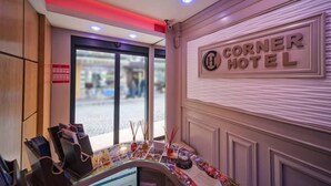 Balcão de recepção no Corner Hotel, com uma placa, divisória de vidro e vista para a rua.