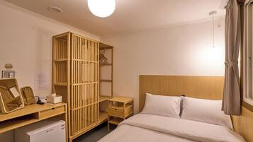 Quarto de hotel com cama, secretária com computador, guarda-roupa e pequeno frigorífico.