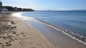 Uma praia com águas cristalinas, areal arenoso e edifícios ao fundo.