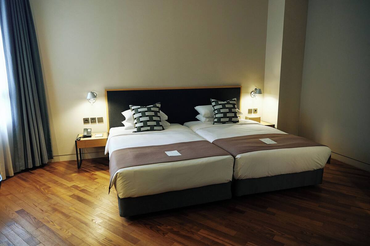 Uma cama de casal com cabeceira de madeira, duas mesas de cabeceira com abajures, um telefone e um bilhete sobre a cama.