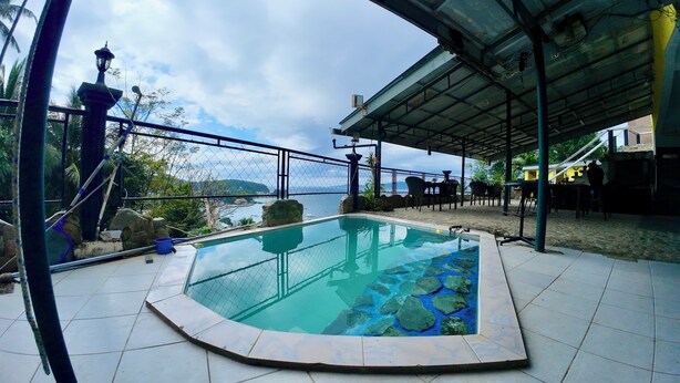 Piscina com vista para o mar, rodeada por um terraço coberto com cadeiras e mesas.