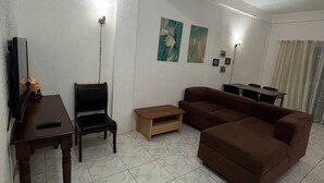 Uma sala de estar com sofá, televisão, mesinha e uma cadeira.