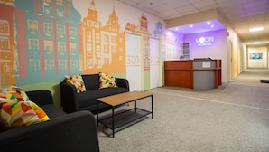 Um saguão de hotel com balcão de recepção, sofás, mesa de centro e um mural colorido de edifícios.