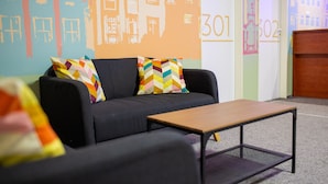 Uma sala de estar moderna com um sofá preto, almofadas geométricas coloridas e uma mesa de centro de madeira.
