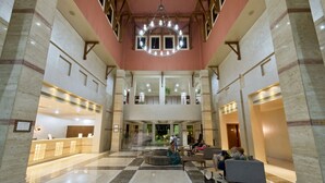 Um hall amplo com chão quadriculado, balcão de recepção, áreas de estar e um lustre decorativo no teto.