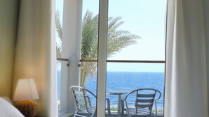 Quarto com cama, mesa de cabeceira com luminária e vista para o oceano através de amplas janelas.