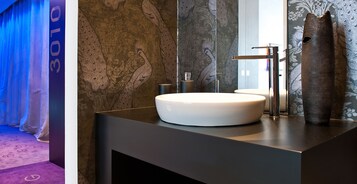Uma casa de banho moderna com uma sanita branca arredondada, um espelho e um vaso decorativo.