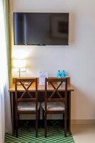 Quarto de hotel com televisão de tela plana na parede, mesa de madeira com duas cadeiras, abajur e duas garrafas de água sobre a mesa.