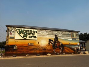 Um motel com um mural de um cowboy montado em um cavalo, um pôr do sol e uma bandeira americana.