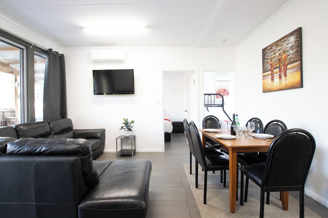 Uma sala de estar moderna com um sofá de couro preto, uma mesa de jantar com cadeiras, uma televisão na parede e um quadro na parede.
