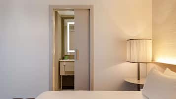 Quarto de hotel com uma cama, luminária de cabeceira e vista para o banheiro.