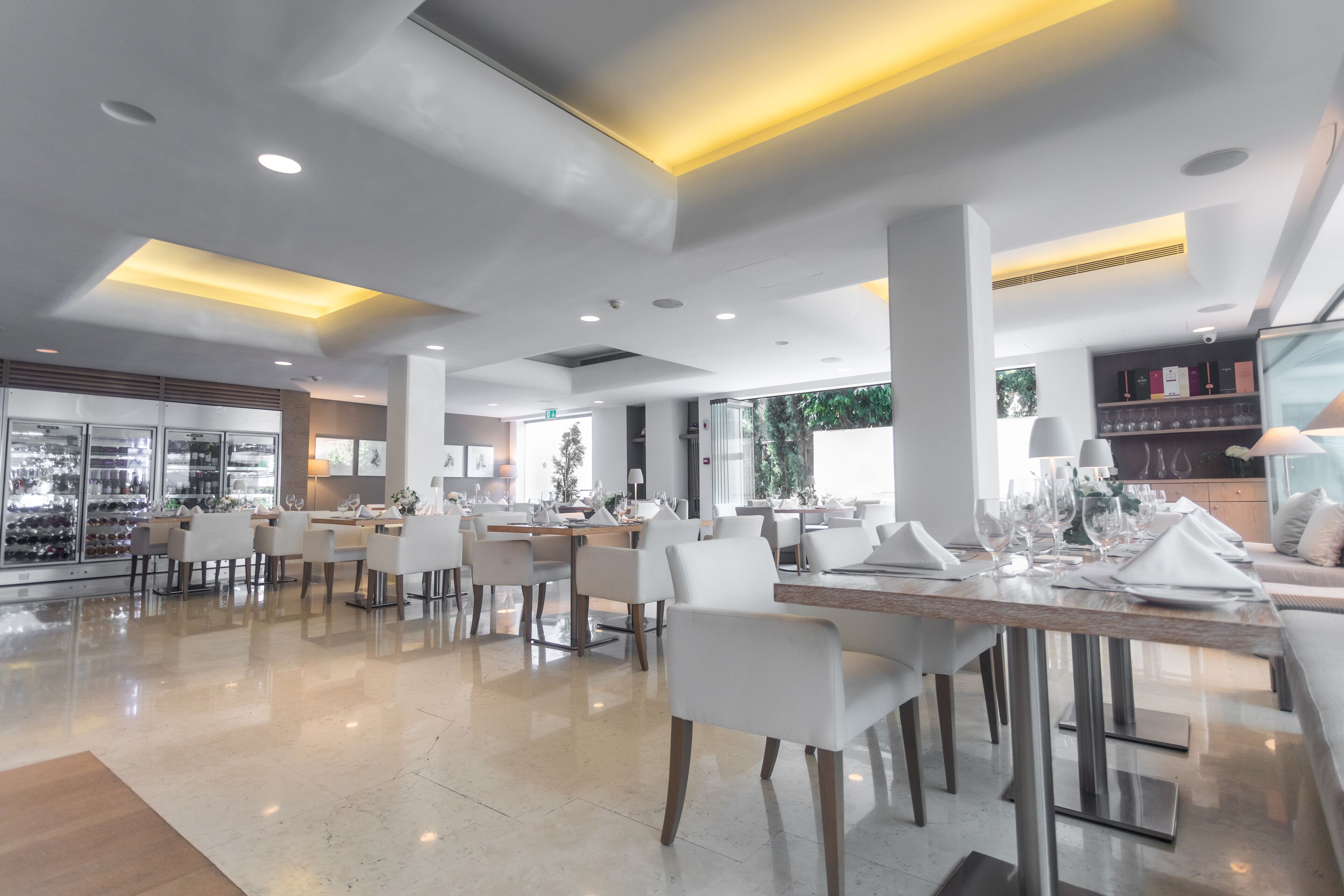 Uma área de jantar ampla e moderna, com pé direito alto, iluminação embutida e piso polido.