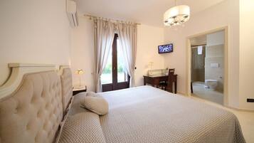 Quarto com cama grande, televisão na parede e banheiro visível através de uma porta aberta.