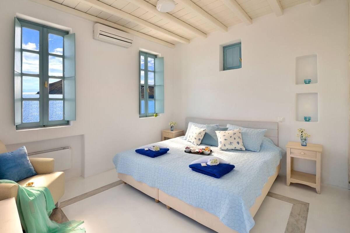 Um quarto com uma cama grande, duas mesas de cabeceira, uma cadeira e uma janela com persianas azuis.