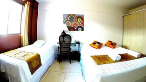 Quarto de hotel com duas camas, uma mesa, uma cadeira e um ornamento colorido na parede.