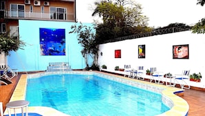 Piscina com borda azulejada, rodeada por espreguiçadeiras e uma pequena mesa.