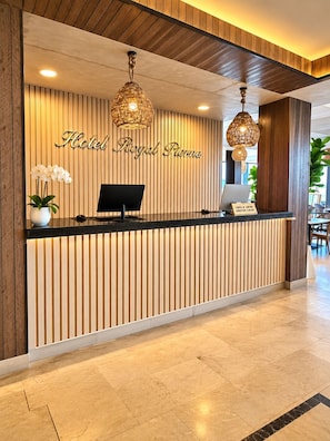 Balcão de recepção de hotel com design moderno, apresentando painel de parede de madeira, balcão e duas luminárias pendentes.