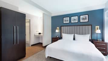 Quarto de hotel com uma cama grande, um guarda-roupa, uma toucador com espelho e três quadros na parede.