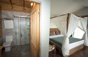 Interior em madeira com box de vidro, sanita branca e cama com dossel.