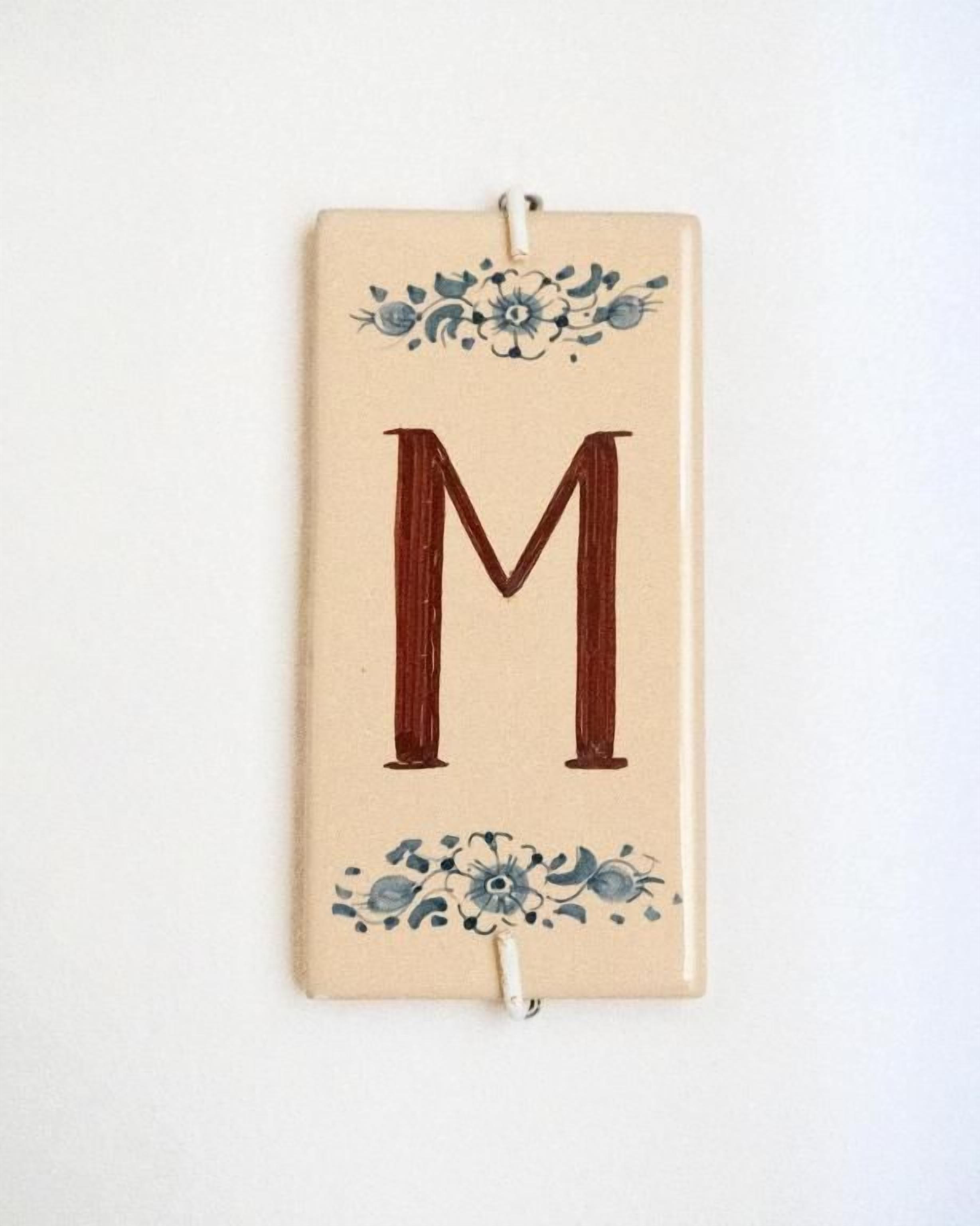 Placa na parede com uma letra 'M' grande e desenhos florais.
