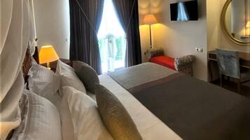 Quarto de hotel com uma cama grande, televisão fixada na parede, escrivaninha com cadeira e janela com cortinas.