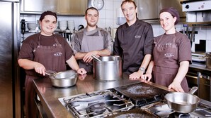 Uma cozinha com eletrodomésticos de aço inoxidável, um relógio e quatro pessoas de avental.